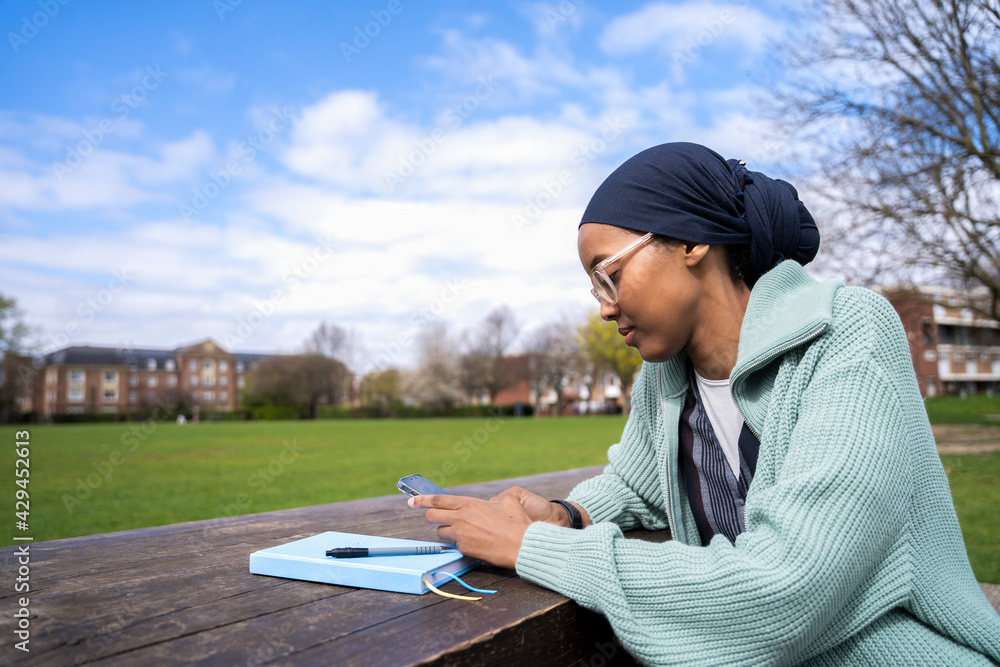 Black Muslim woman in park writing Stock Photo | Adobe Stock