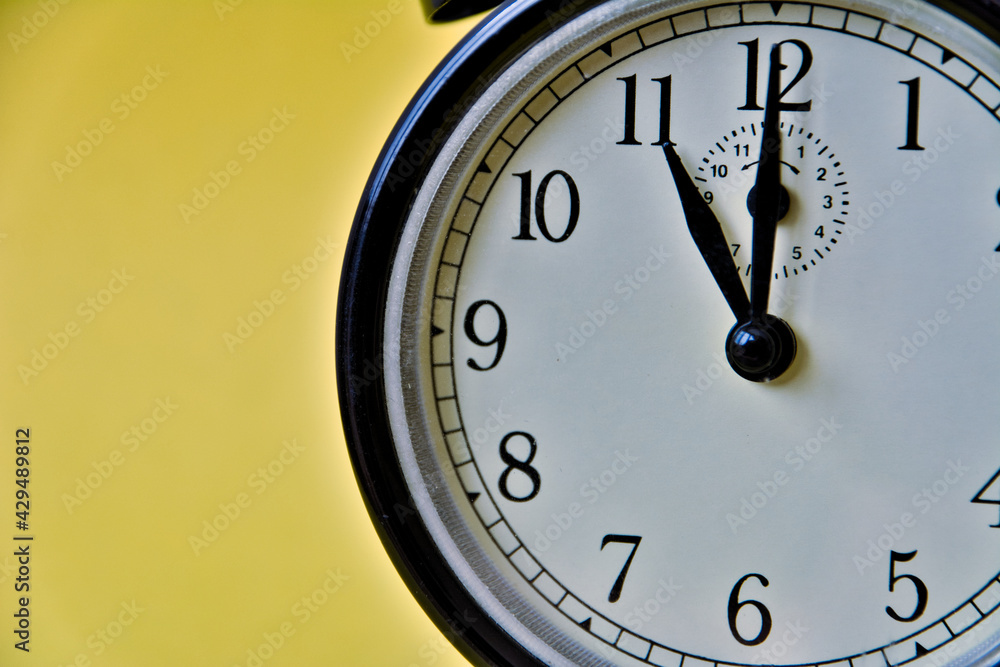 Shot of vintage retro analog clock on yellow background showing 11 o ...