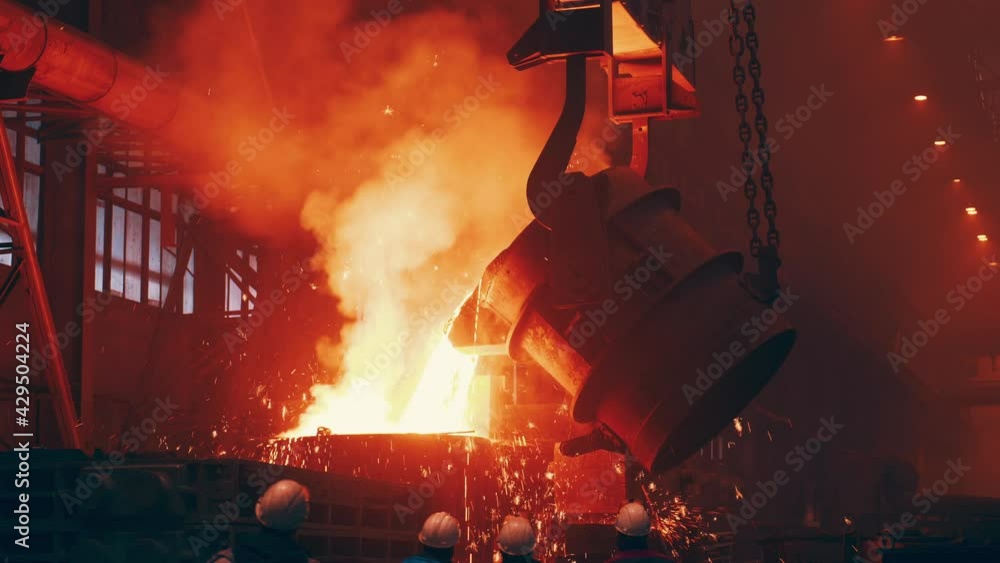 Pouring bright hot liquid steel or metal from ladle in blast furnace ...
