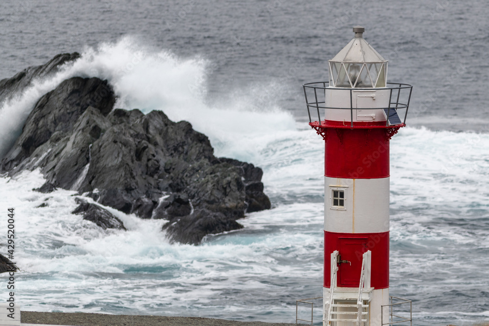 A tall circular lighthouse tower has horizontal red and white colours ...