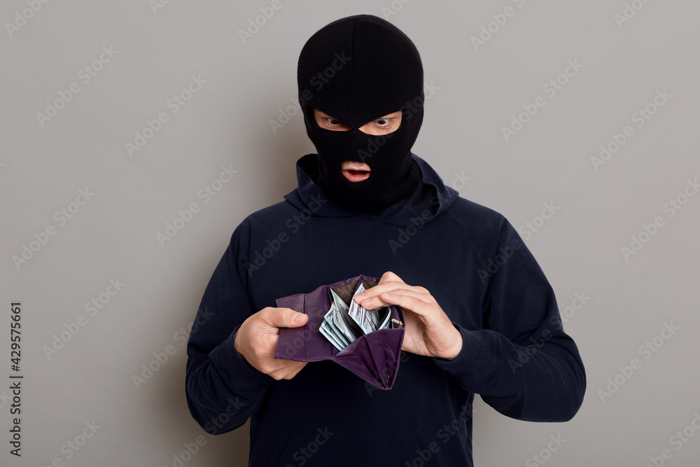 Surprised man thief dressed in robber mask holding open wallet in his ...