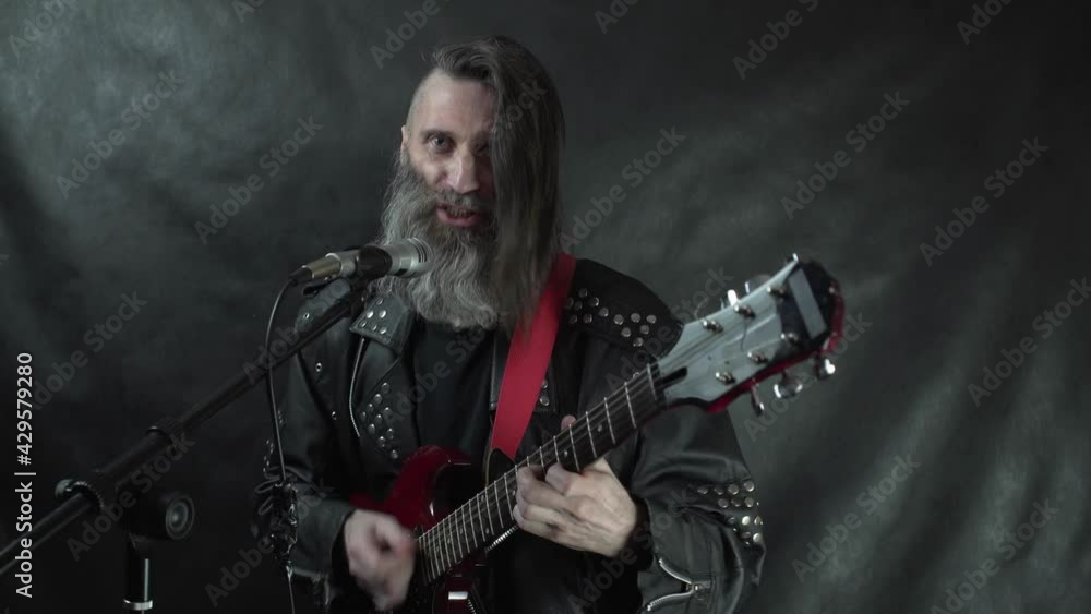 Bearded long-haired rock musician in leather jacket plays red electric ...