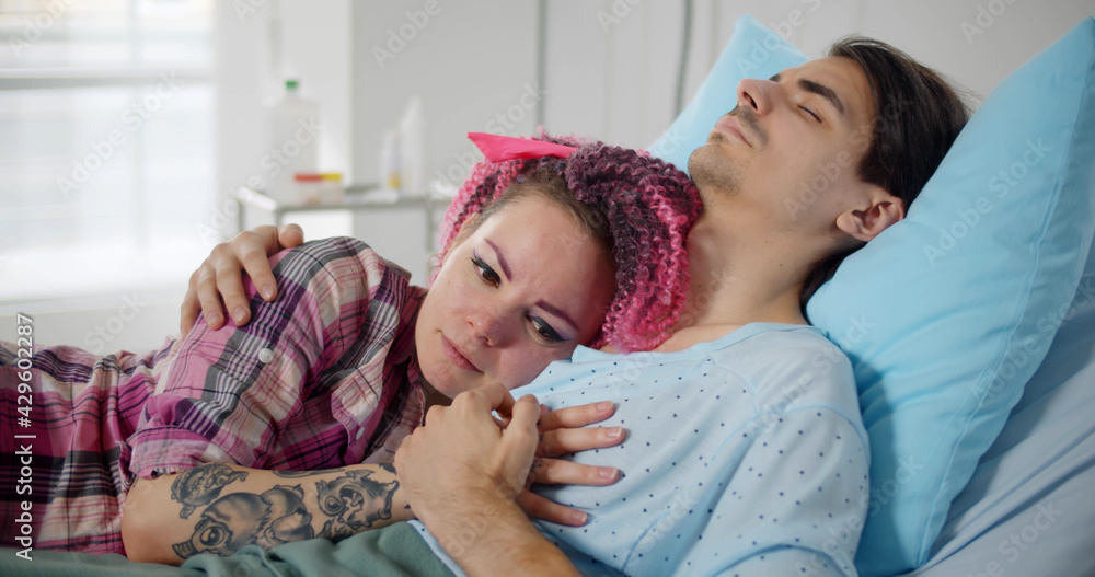 Worried and sad young woman hugging sick husband sleeping in hospital ...