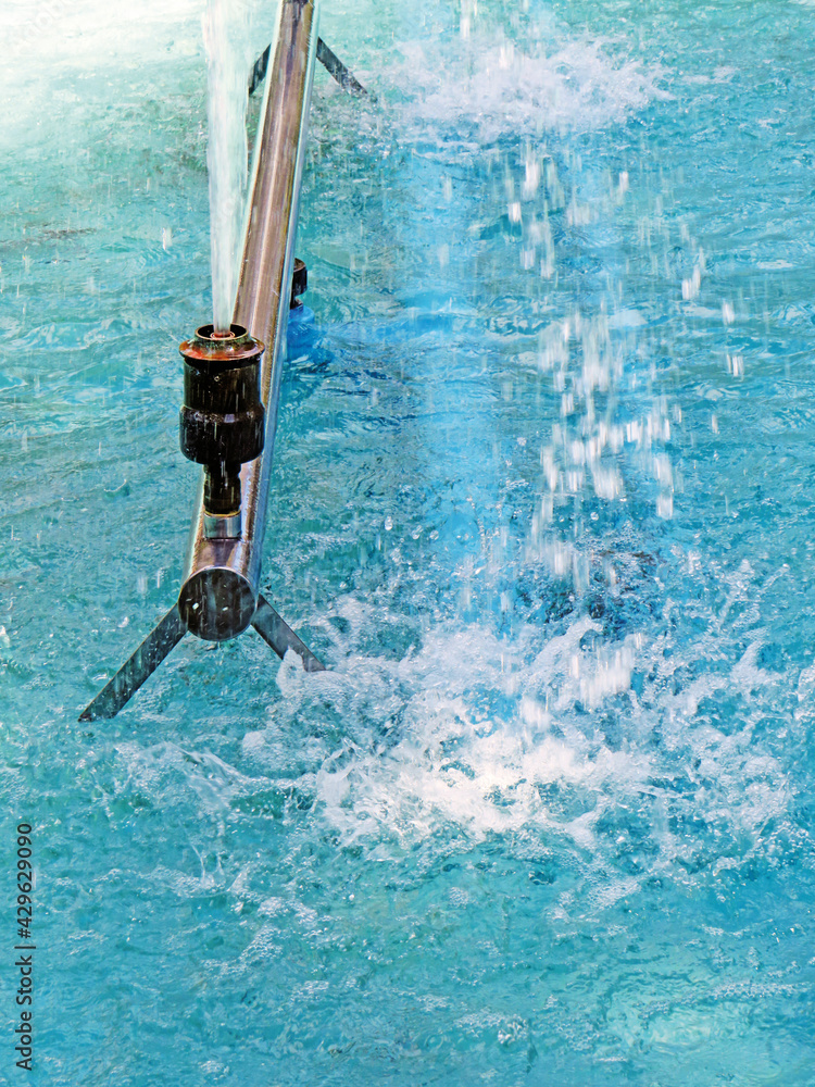 Detail of water jet spout in fountain with blue water and reflections ...