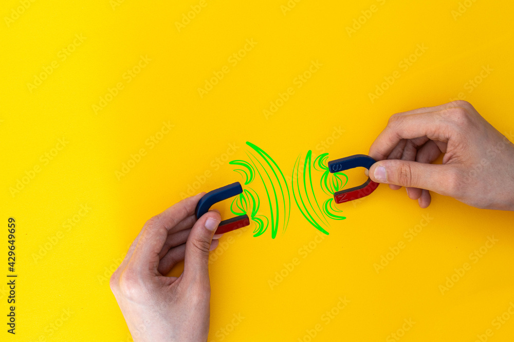detail of hands holding two blue and red horseshoe-shaped magnets ...