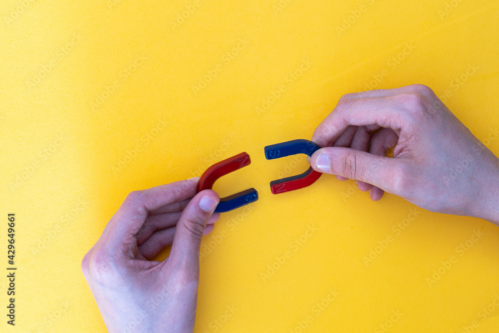 detail of hands holding two blue and red horseshoe-shaped magnets ...