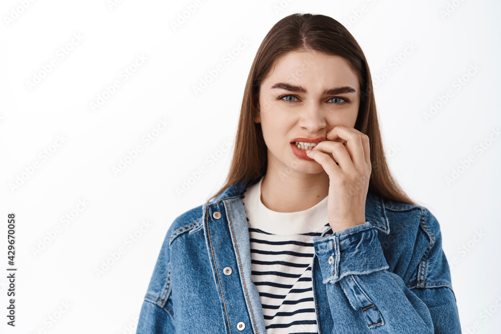 Nervous girl bites her finger nails and looks worried at camera ...