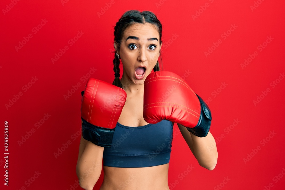 Young brunette girl using boxing gloves afraid and shocked with ...