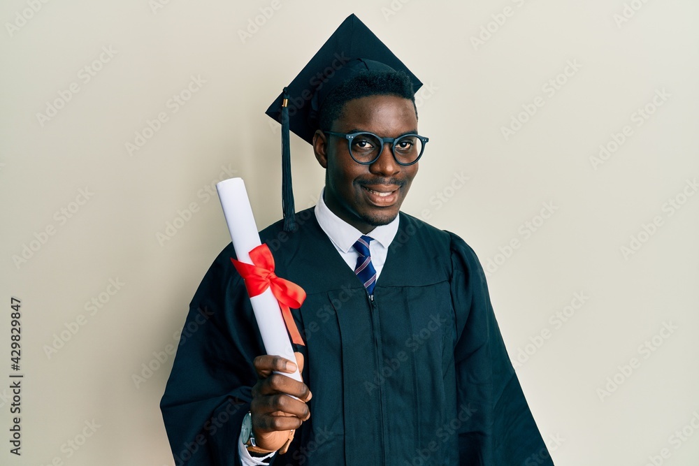 Handsome black man wearing graduation cap and ceremony robe holding ...