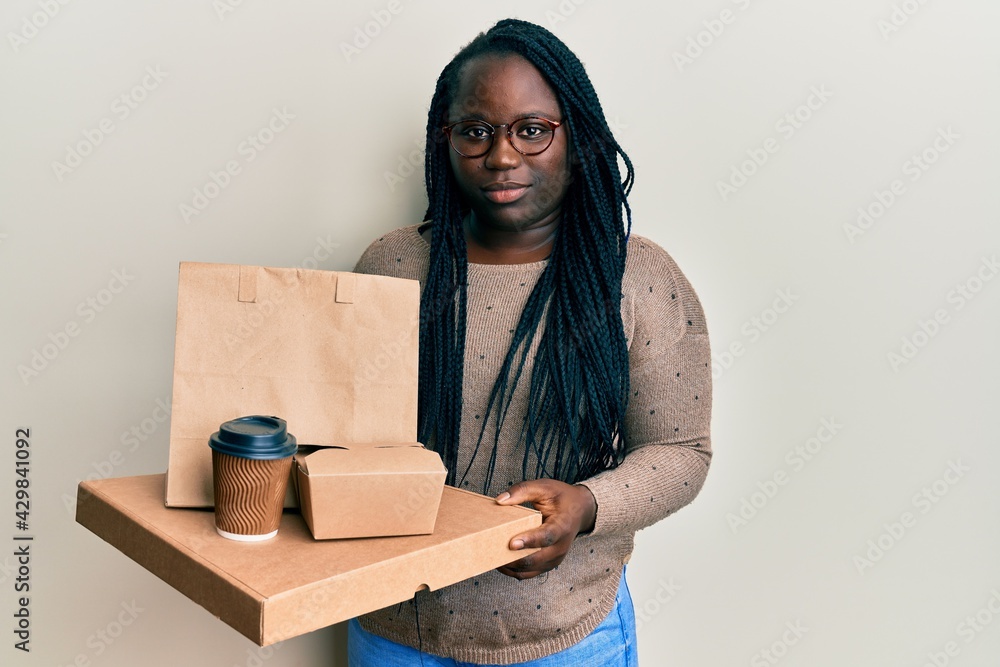 Young black woman with braids holding take away food relaxed with ...