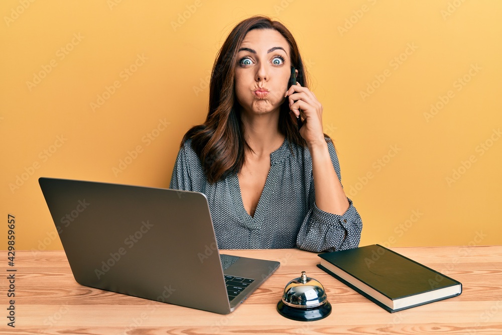 Young brunette woman working at hotel reception talking on the phone ...