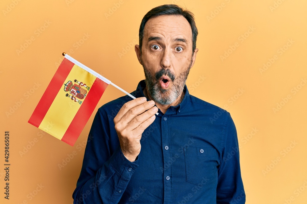 Middle age hispanic man holding spain flag scared and amazed with open ...