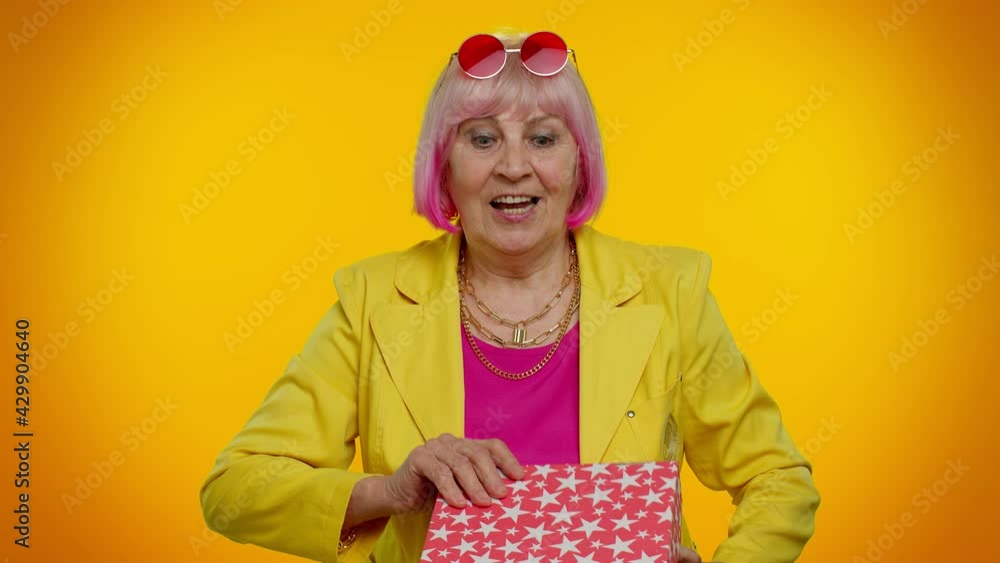 Vidéo Stock Elderly granny woman in yellow jacket opening gift box ...