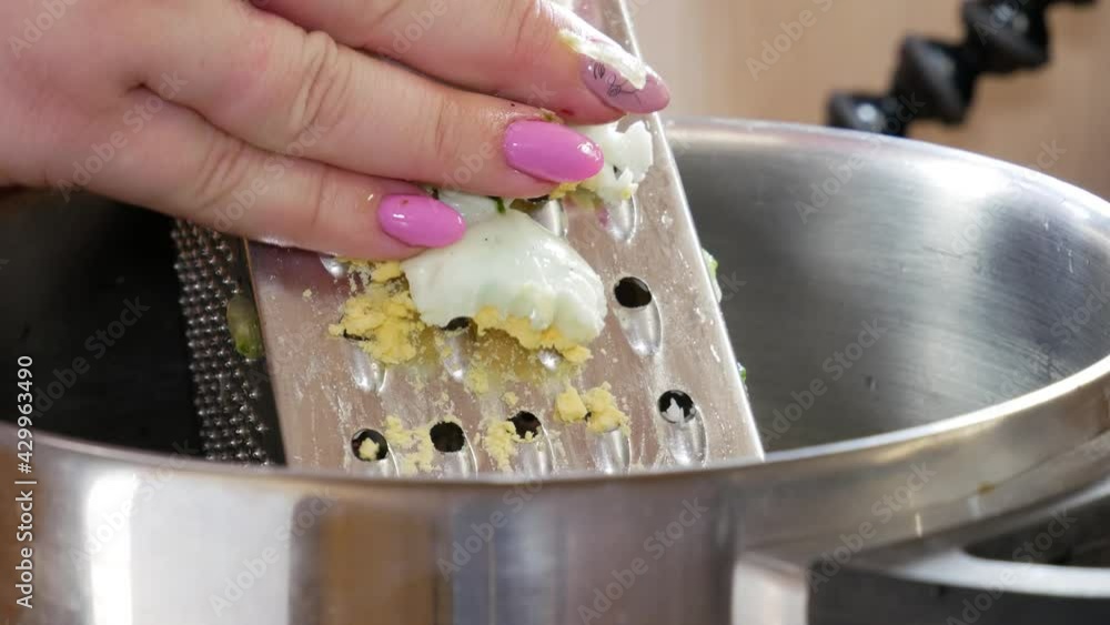 Female hands grating freshly hard-boiled egg on iron grate, static view ...