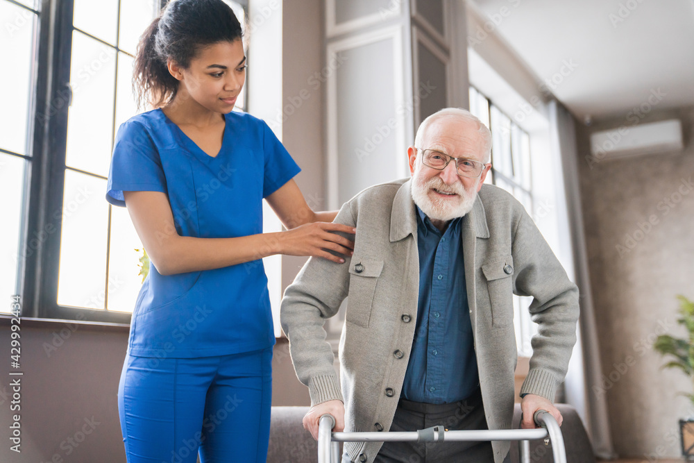 Foto de Man using walker rehabilitation at home. Nurse helping disabled ...