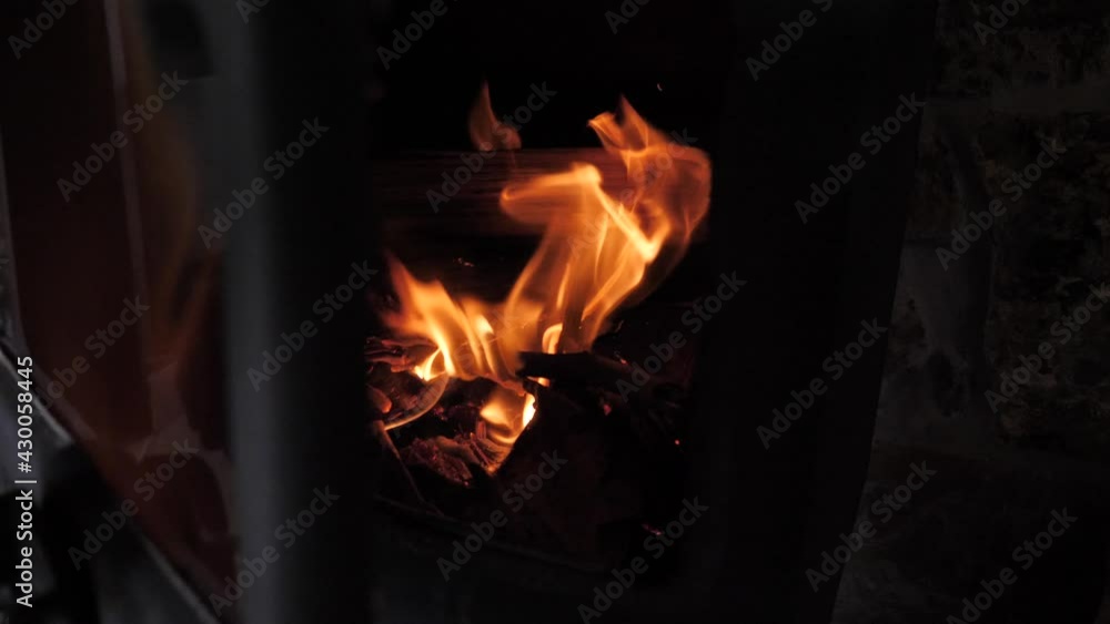 Hand opening metal door of small cabin fireplace as red hot fire burns ...