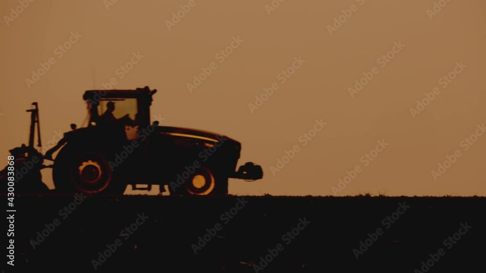 Silhouette of tractor drives across field at sunset, side view. Stock ...
