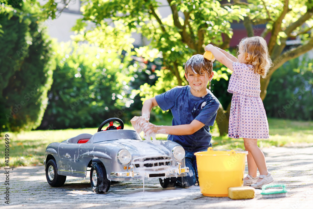 Two happy children washing big old toy car in summer garden, outdoors ...