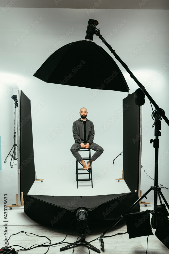Male model sitting on a chair on a white background surrounded by a ...