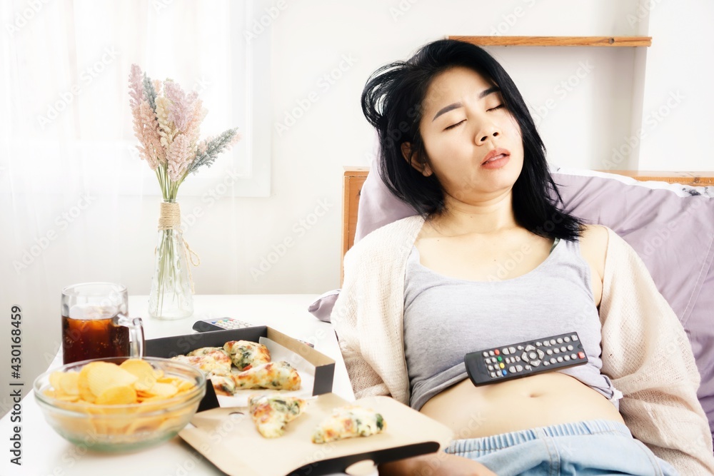 Asian woman sleeping in bed after eating pizza, potato chips and soda ...