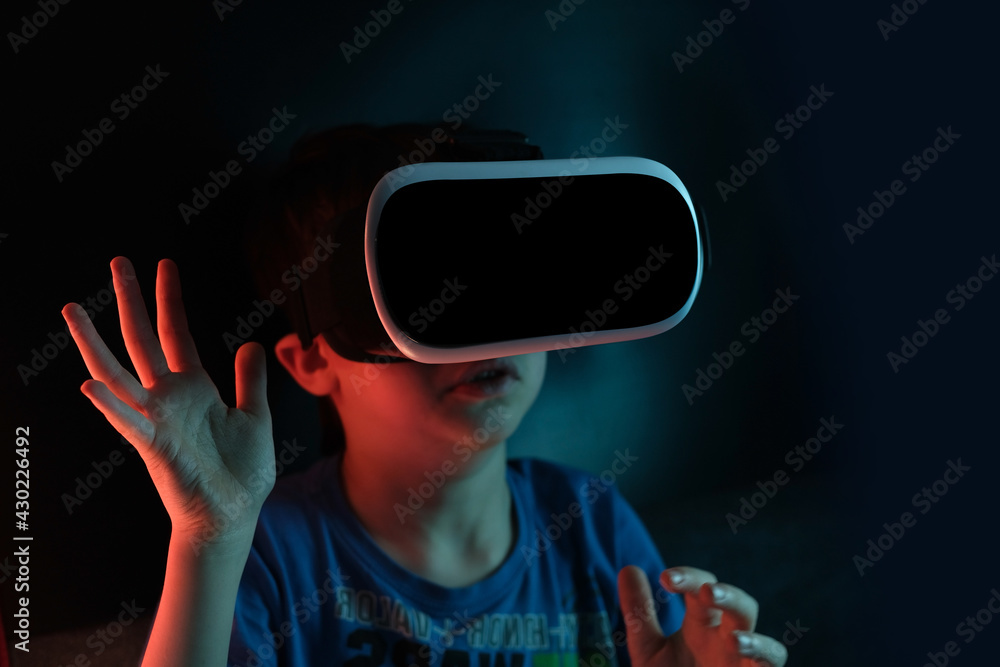 boy, child in dark room with neon lights in modern VR glasses ...