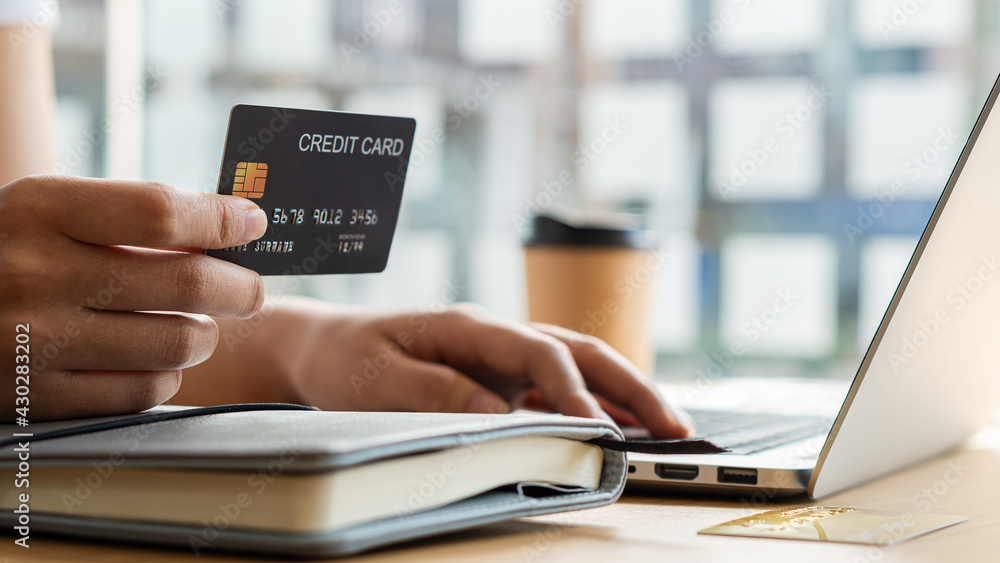 A young woman holds a plastic credit card on her computer in online ...