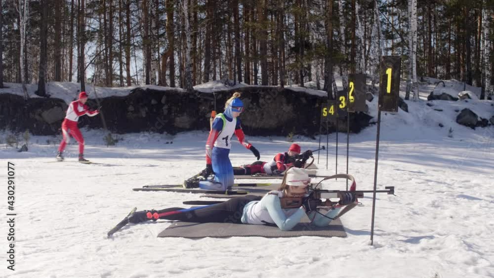 Male and female biathletes shooting with rifles in prone positions at ...