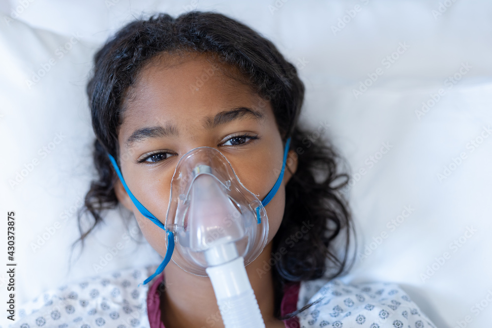 Portrait Of Sick Mixed Race Girl Lying In Hospital Bed Wearing Oxygen