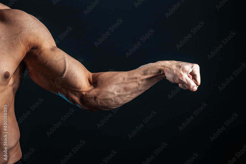 tense arm clenched into fist, veins, bodybuilder muscles on a dark ...