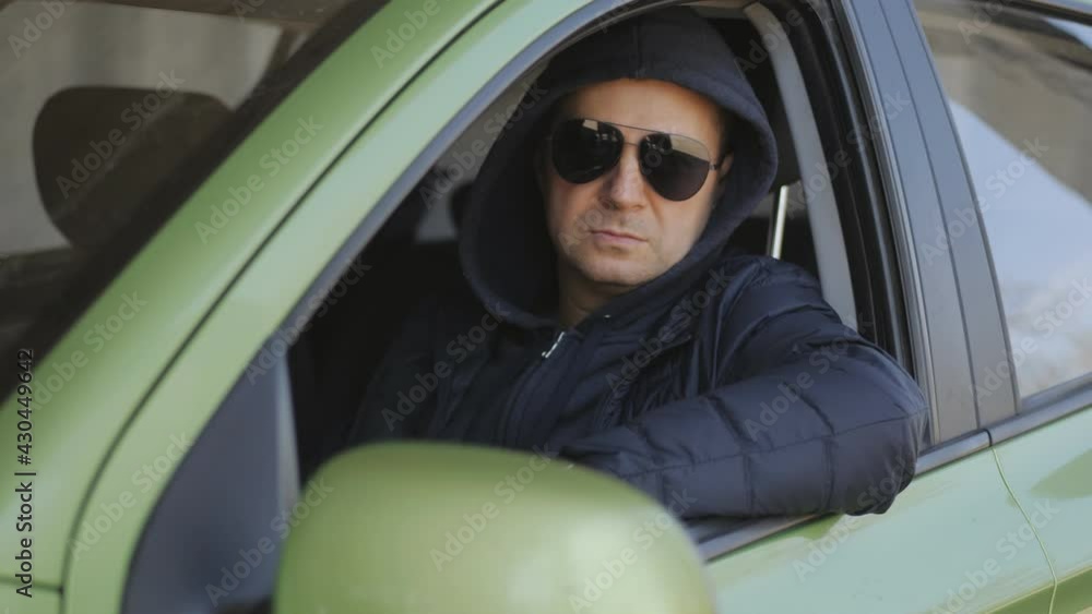 A suspicious man in a black hoodie with a hood and black glasses sits ...