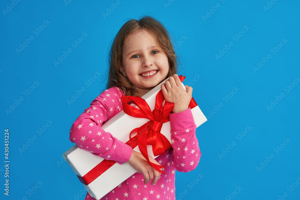 Little cute girl with a gift box with a red ribbon on a blue background ...
