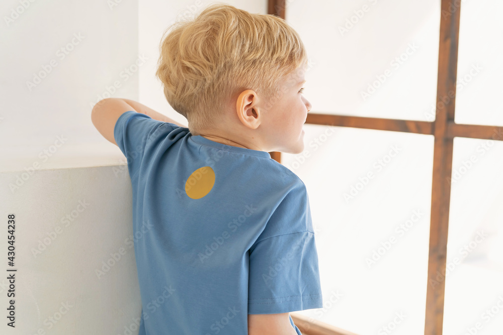 little boy with blond hair, sitting with his back turned away from ...