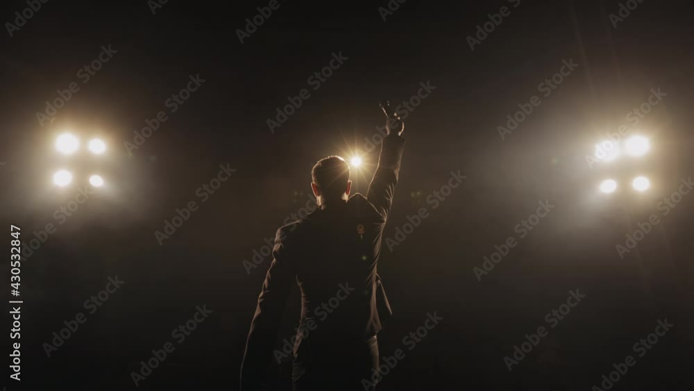 The man is coming on stage and raising up the microphone. He's wearing ...