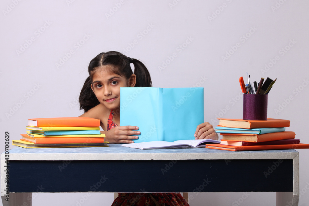 little Indian or asian school girl reading book over study table. stack ...