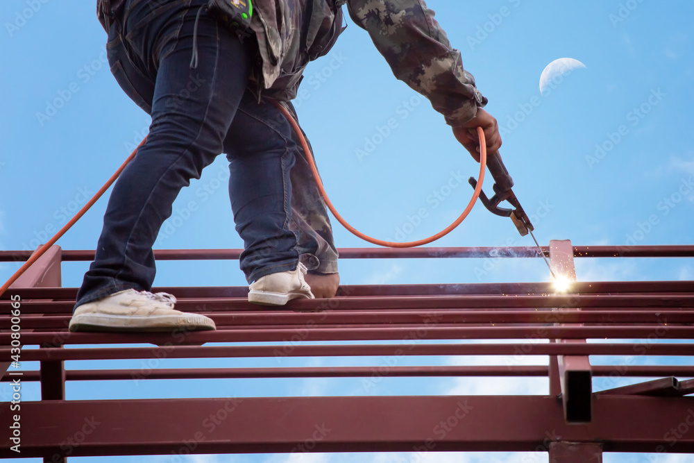 Red painted steel roof truss, with roof welders working at dangerous ...