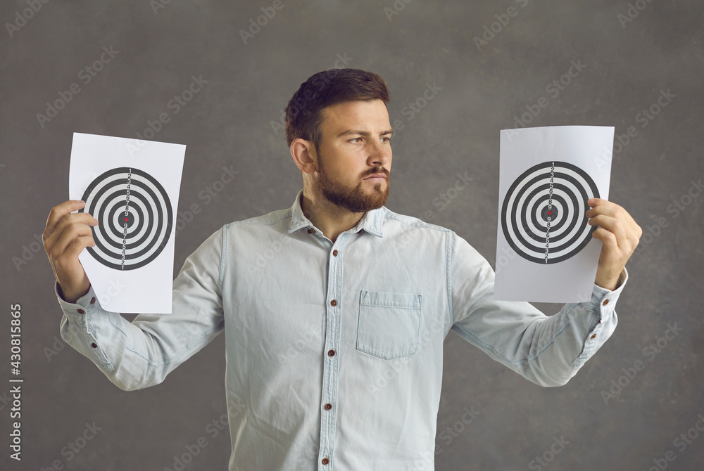 Serious young man holding two sheets of paper with shooting targets ...