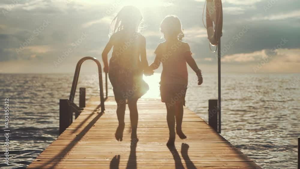 Two sweet young girls friends holding hands running towards sunset ...