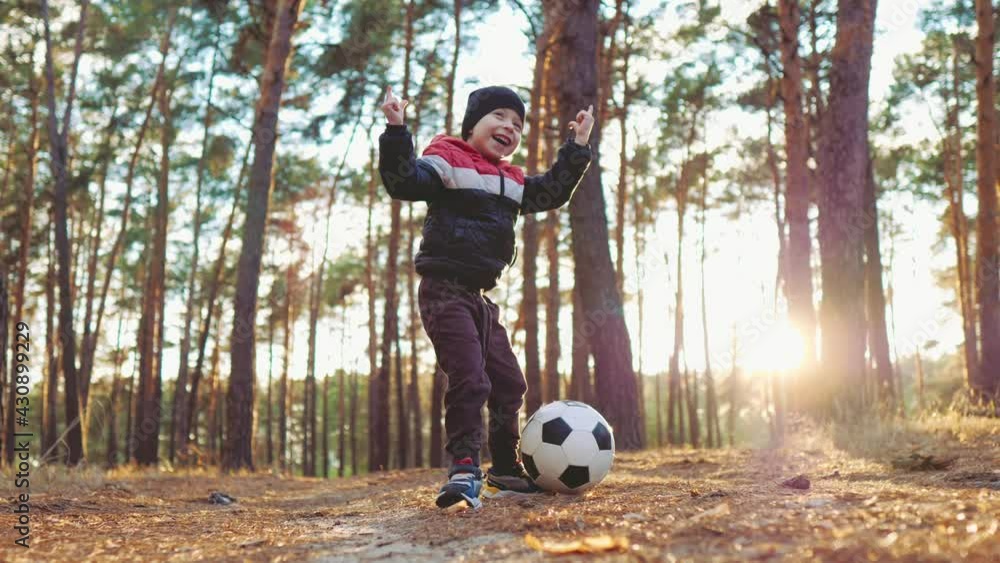 Childhood dream. Little boy playing football soccer in the pine forest. Boy child training ...
