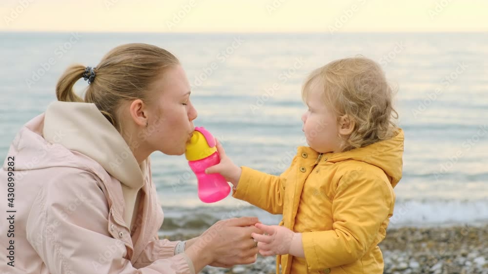 kind and caring child girl in yellow jacket invites her mother to drink ...