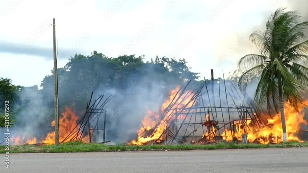 In bright flames burning indian hut made of wood and dried palm leaves ...