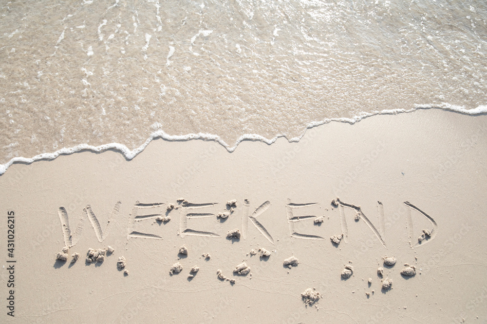 Word "WEEKEND" hand written in the sand. Close up sand texture on beach ...