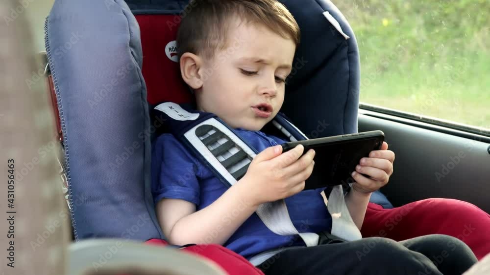 Little boy sitting in a car seat watching a cartoon on the phone ...