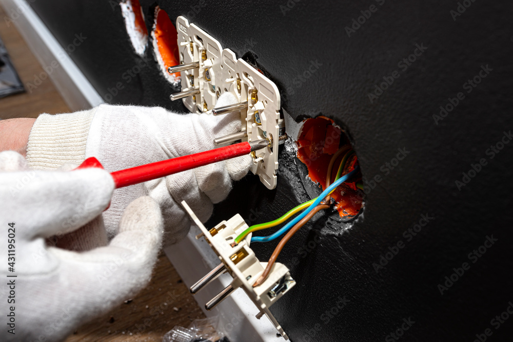 An electrician uses a red screwdriver to screw a double grounded ...