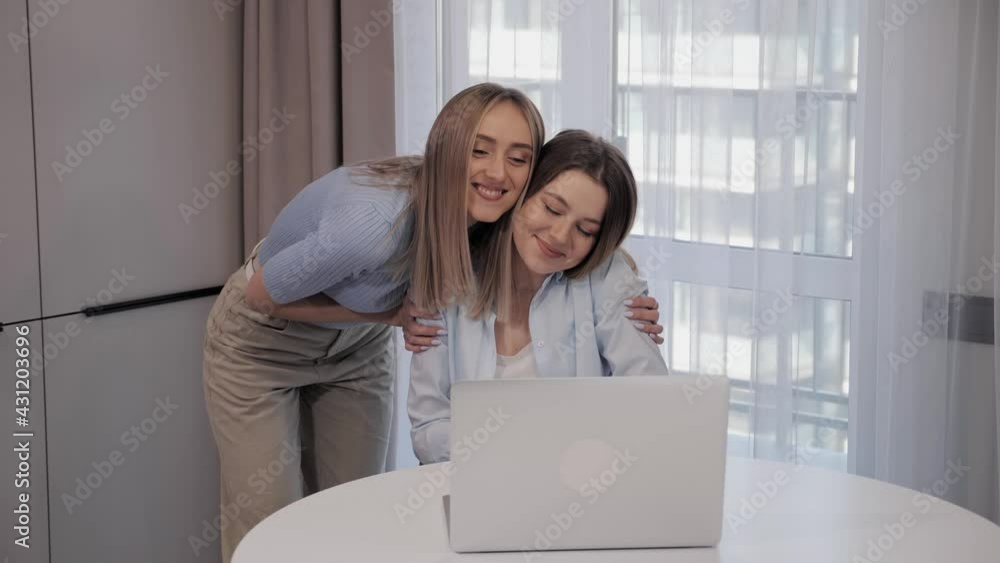 Two beautiful lesbian girls look at the laptop, gently hug looking for ...