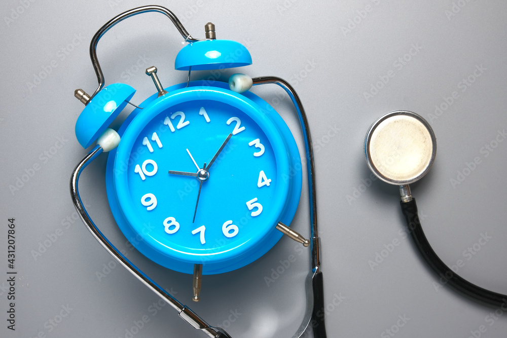 A picture of clock and stethoscope on grey background. Healthcare check ...