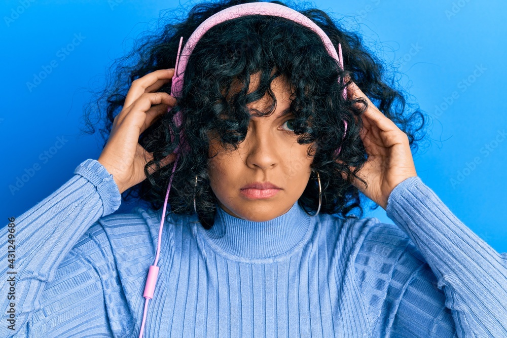 Young hispanic woman listening to music using headphones skeptic and ...