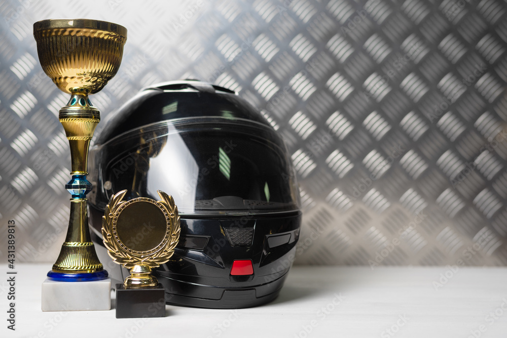 A motorcycle helmet, award trophy cup and golden medal on the metal ...