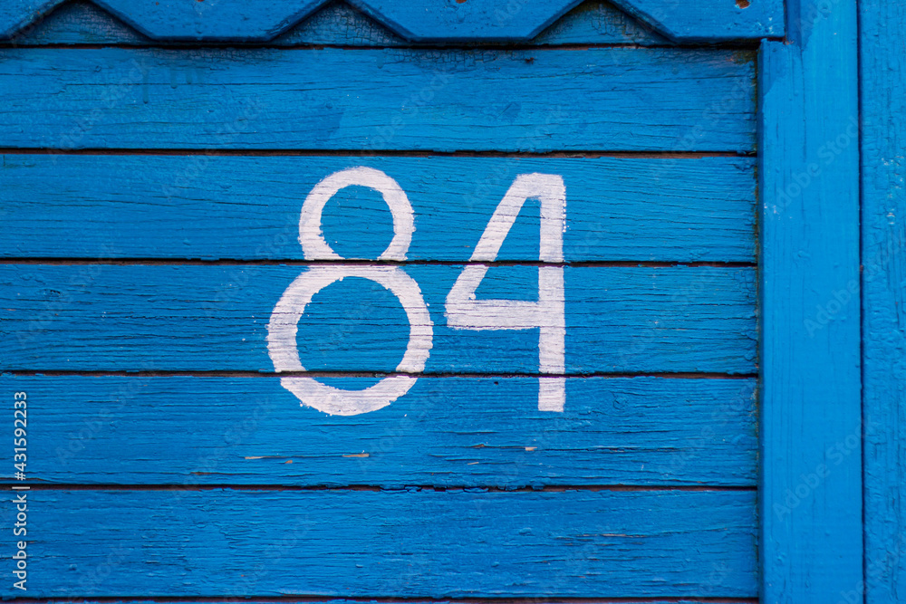 House number 84. The numbers are painted in white paint using a stencil ...