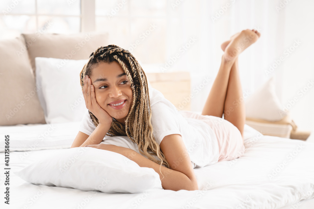Cheerful young african-american woman relaxing peacefully on white bed ...