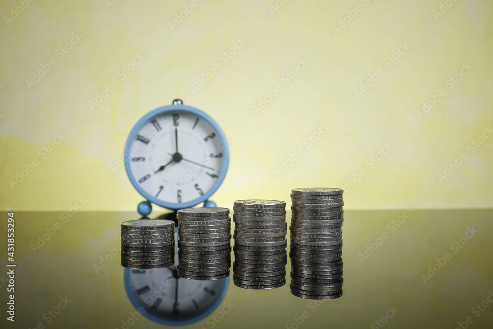 Stacked coins with an alarm clock at the back creating a blur effect ...